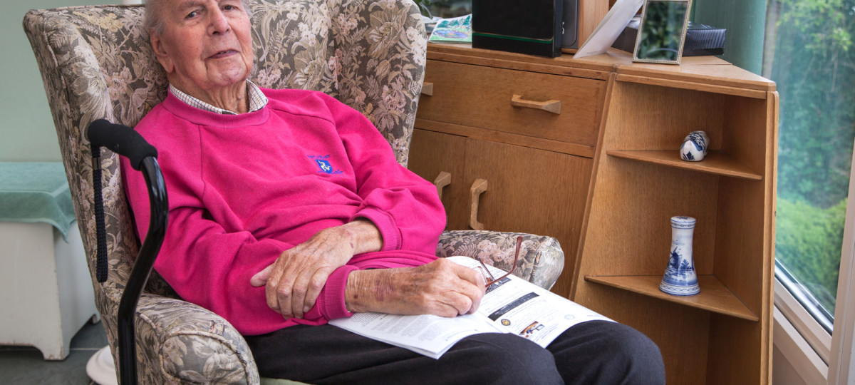 95 years old English man in domestic interior, reading local life ...
